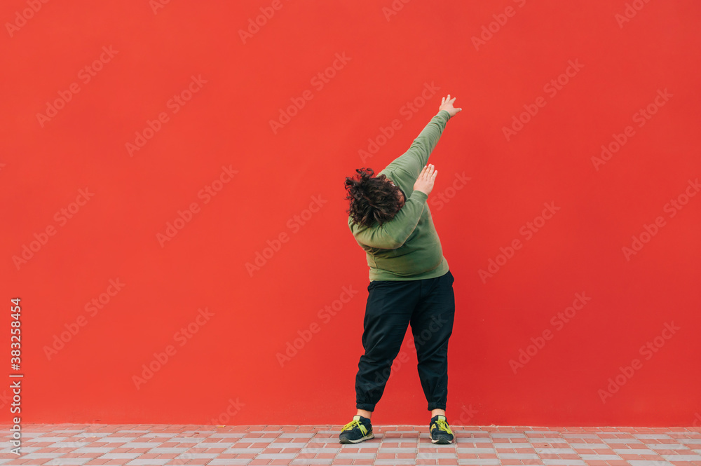 Fat man in casual clothes stands on a red background and dances a dab ...