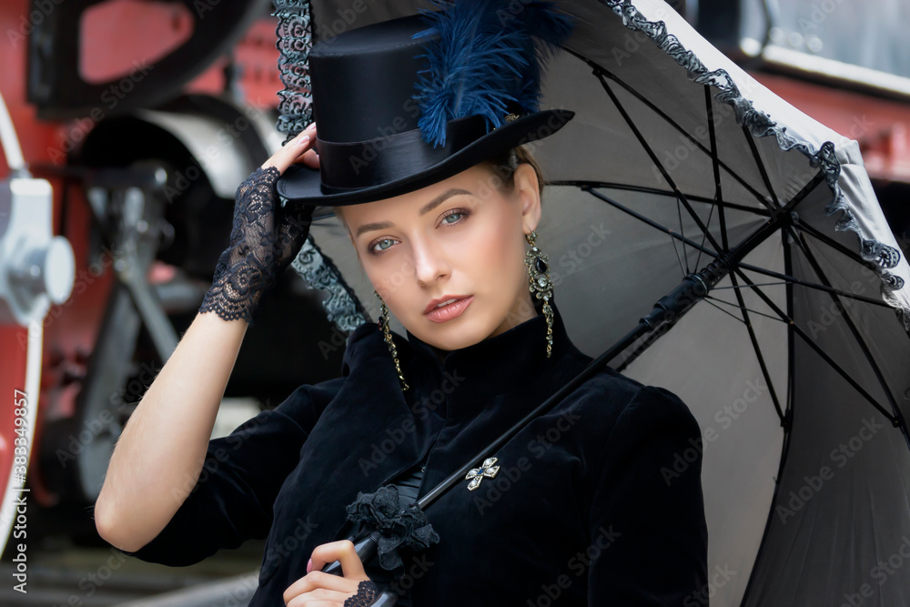 Steampunk girl in a black dress and hat near an old steam locomotive ...