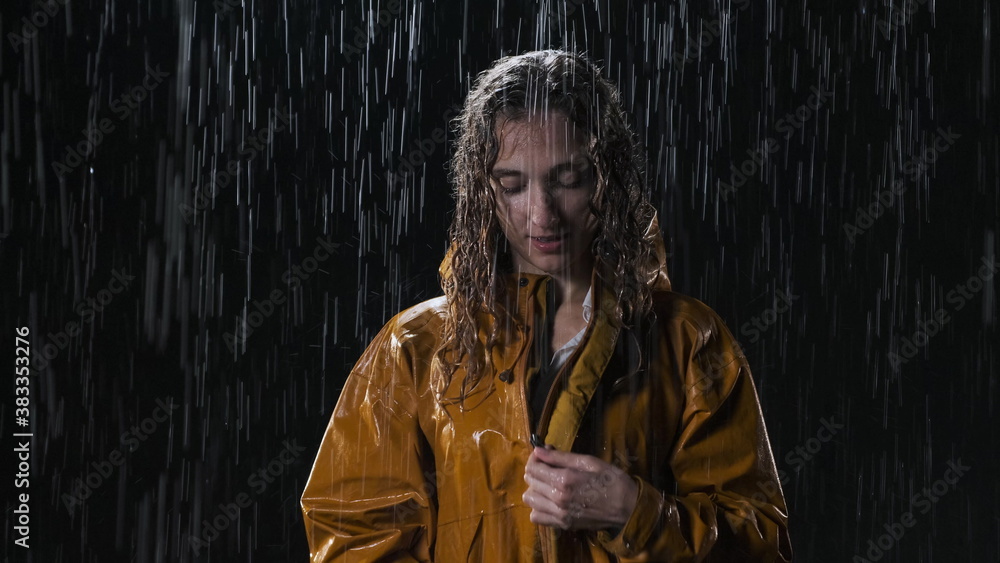 Satisfied woman in yellow raincoat puts on hood raincoat. It is pouring ...