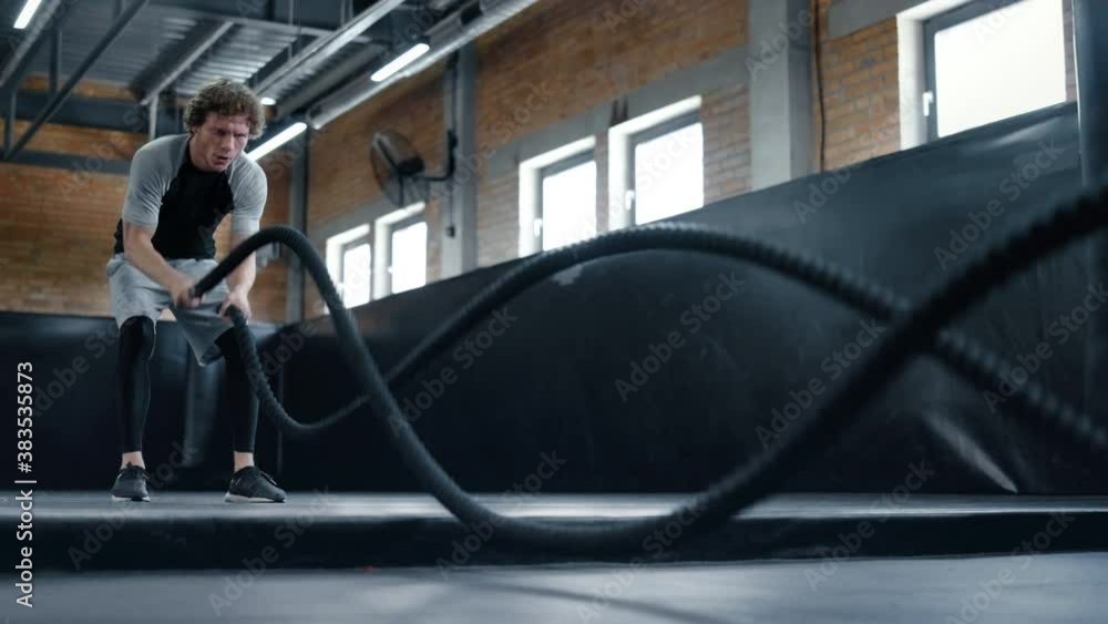 Aggressive kickboxer doing workout at gym. Sportsman using battle ropes ...