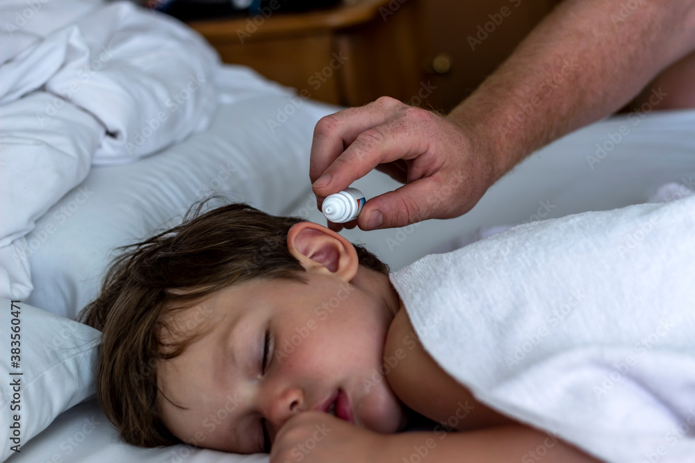 Medical pipette with a drop of medication over the boys ear. Man ...
