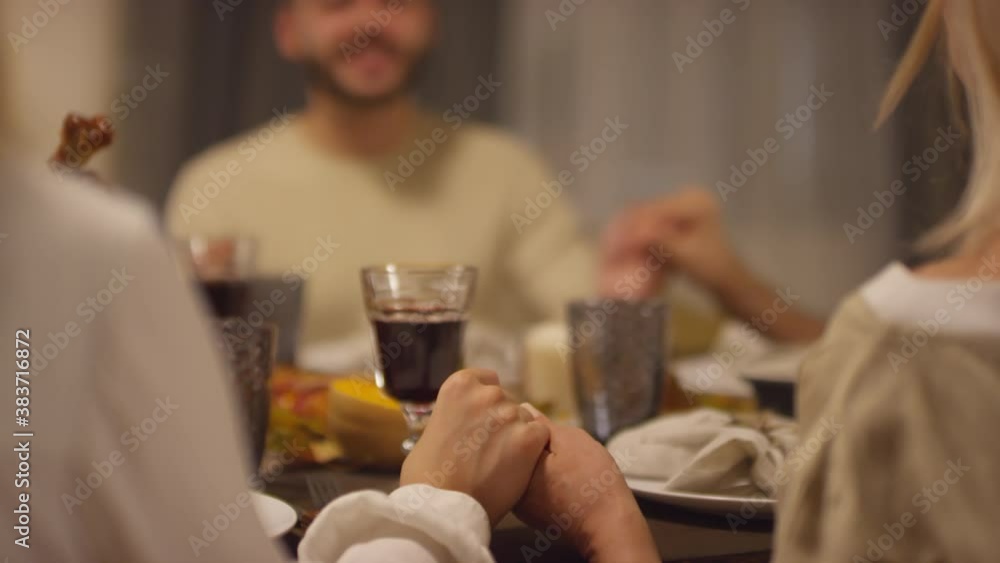 Modern family sitting together at dining table holding hands and ...