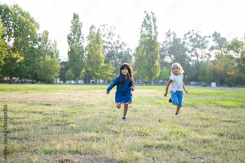 Excited little girls running on grass to camera, having race in park ...
