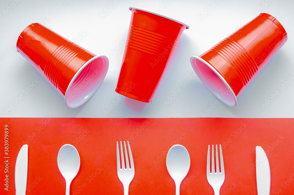Single use white plastic cutlery and red plastic glass on a red and ...