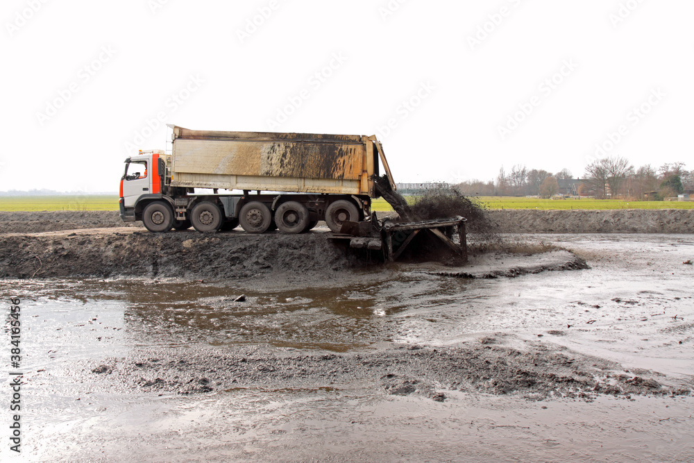 Large truck with tipper trailer unloads its freight of dredging spoil ...