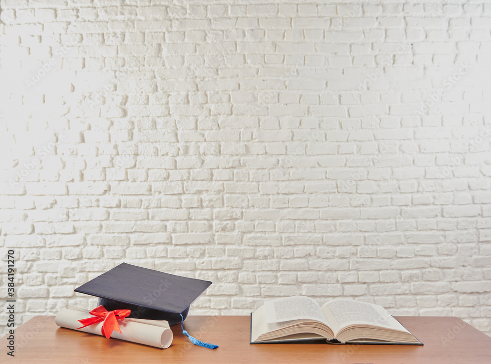 Graduated cap and laptop on the wooden table, white brick background ...
