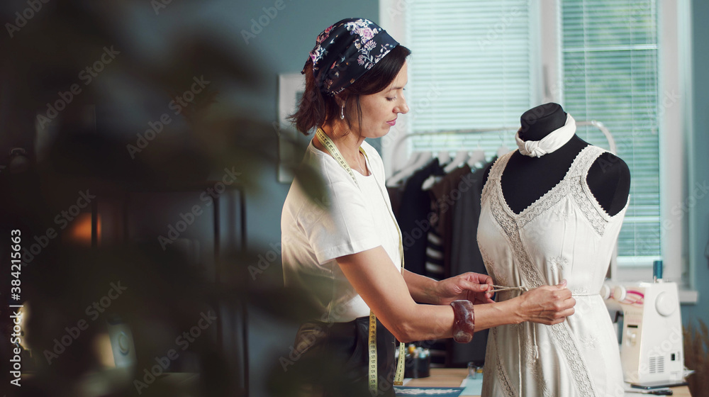 Female dressmaker adjusting dress on mannequin in sewing studio ...