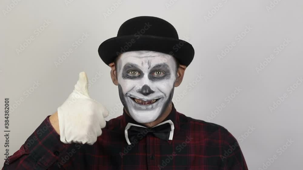 A horrible man in clown makeup smiles and shows a thumb up. A scary ...