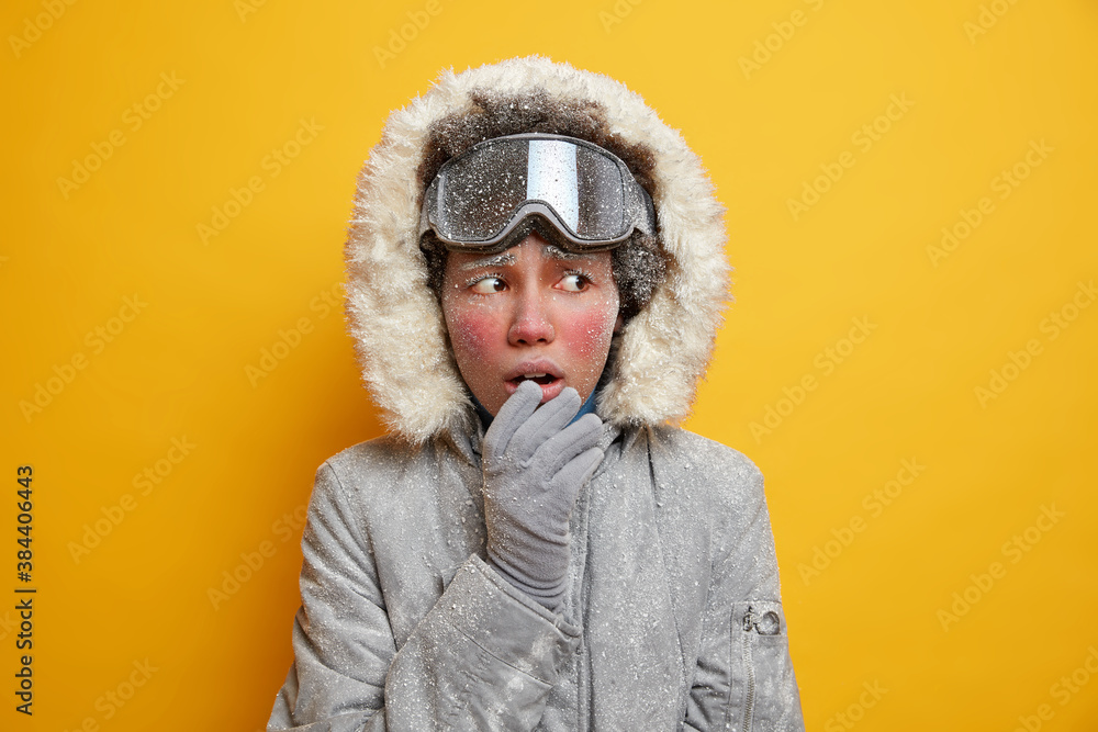 Foto de Puzzled ethnic woman with face covered by ice feels cold looks ...