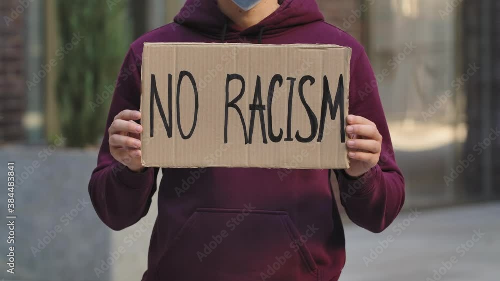 NO RACISM on a cardboard poster in the hands of male protester activist ...