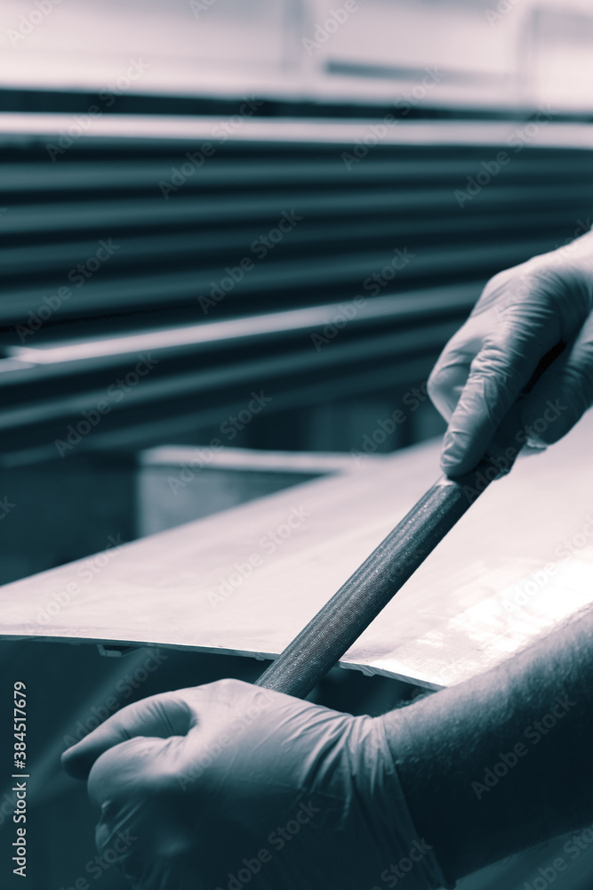 Man filing deburring a metal panel with a file. With colour toning ...