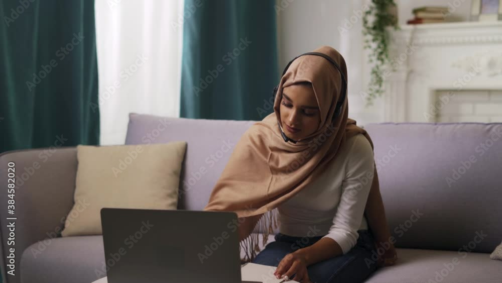 Muslim young woman in hijab scarf and headset is studying online ...