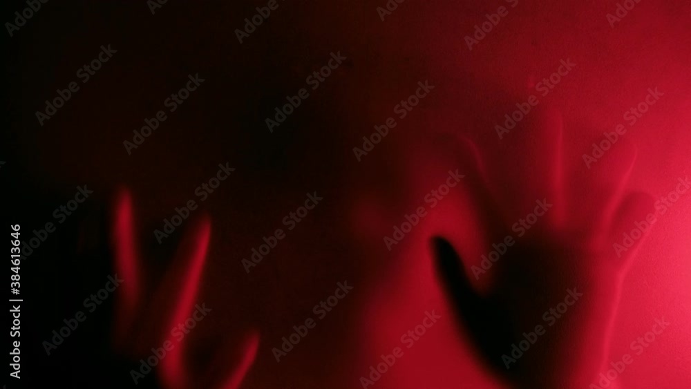 Defocused Possessed person scratching glass with hands with red light ...