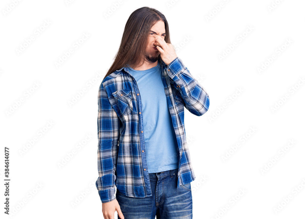 Young adult man with long hair wearing casual shirt smelling something ...