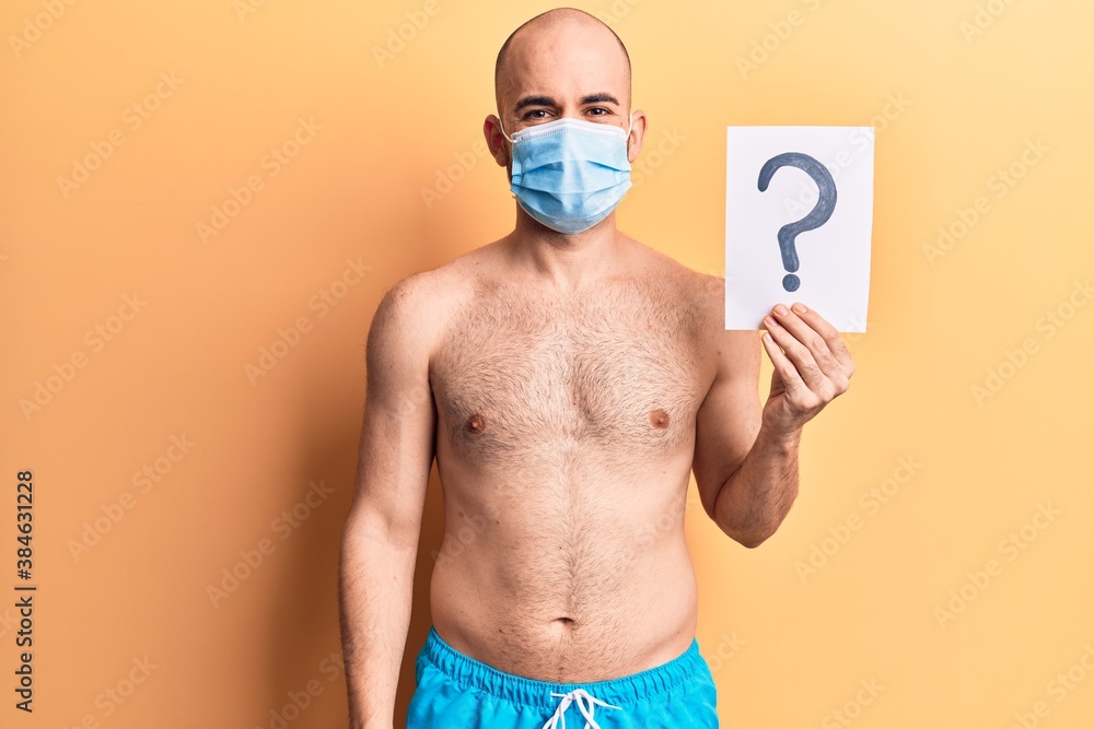Young handsome bald man wearing swimwear and medical mask holding ...