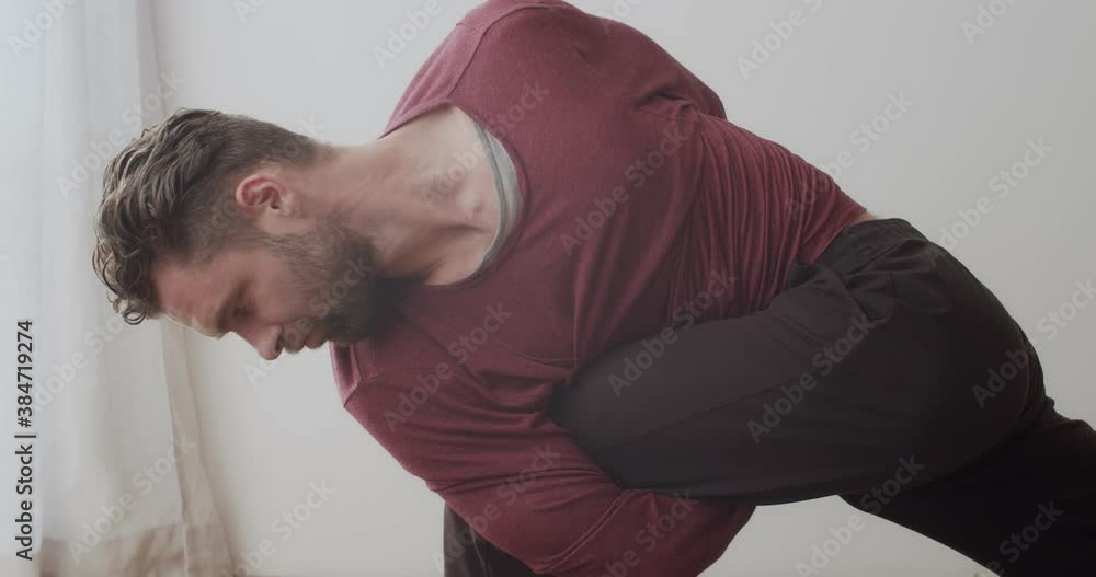 Close up detailed shot of man standing in twisted yoga pose indoors ...