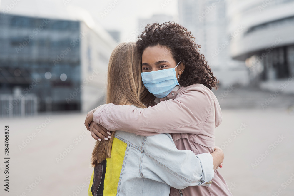 Meeting of two happy friends hugging in the street wearing protective ...