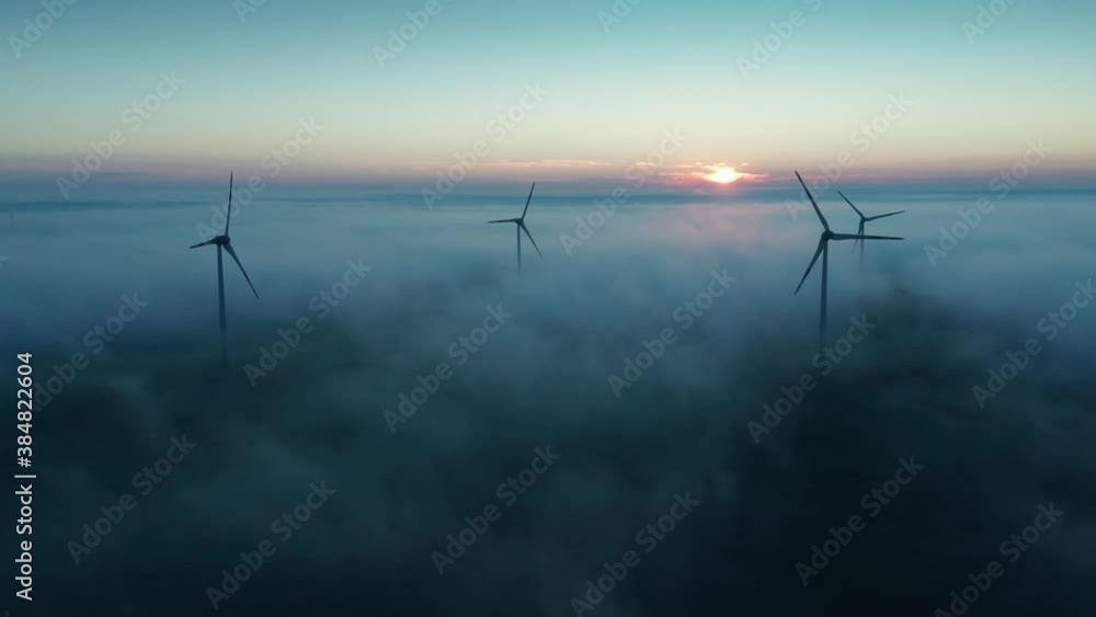 Wind turbine at sunrise in heavy fog. Wind farm generating green energy ...