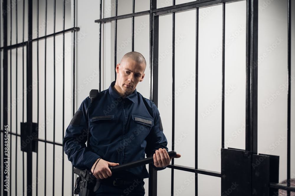 A strict prison guard in uniform guards cells with prisoners in a ...