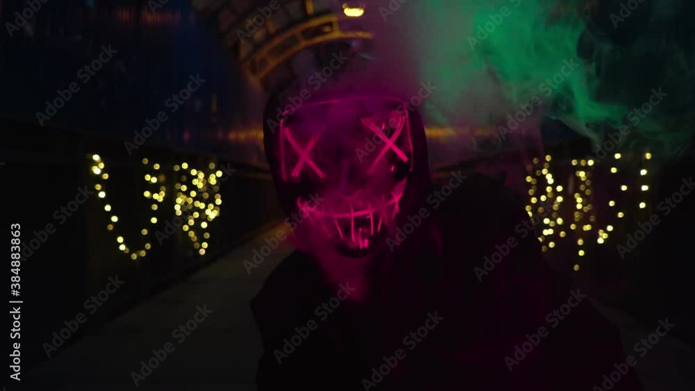 The man in the neon mask blows smoke. Thick green and pink smoke. Scary ...