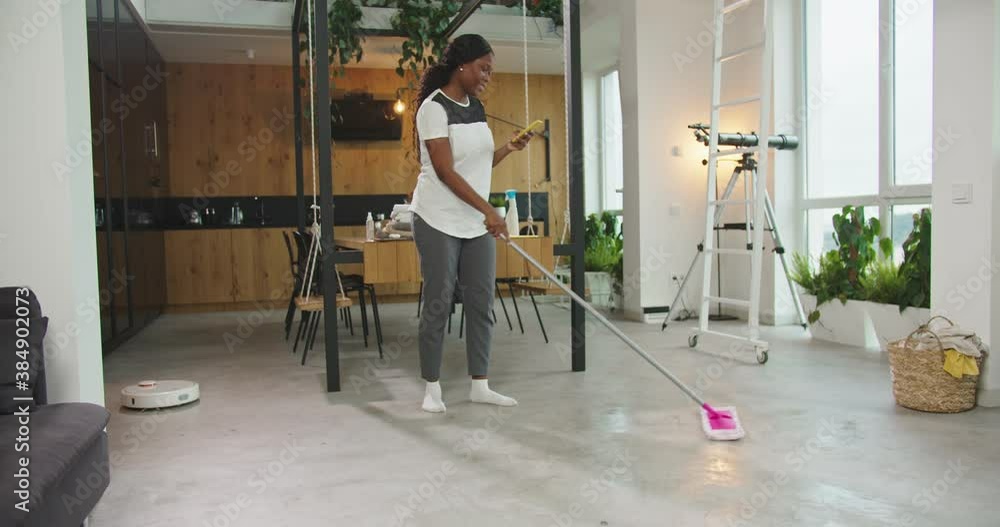 Beautiful african american woman mopping floor in living room with mop ...