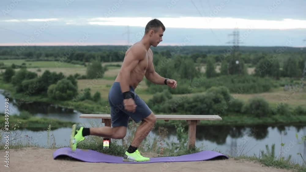Young bodybuilder in blue shorts trains by the river and does step ...