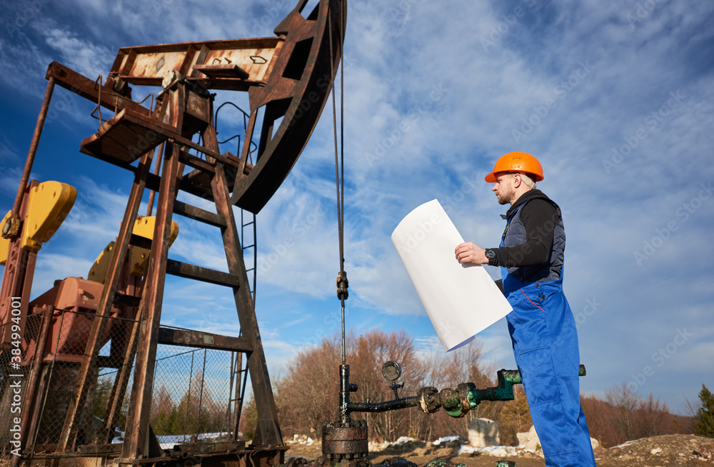 Side view of oil worker holding plan of oil field at petroleum pump ...