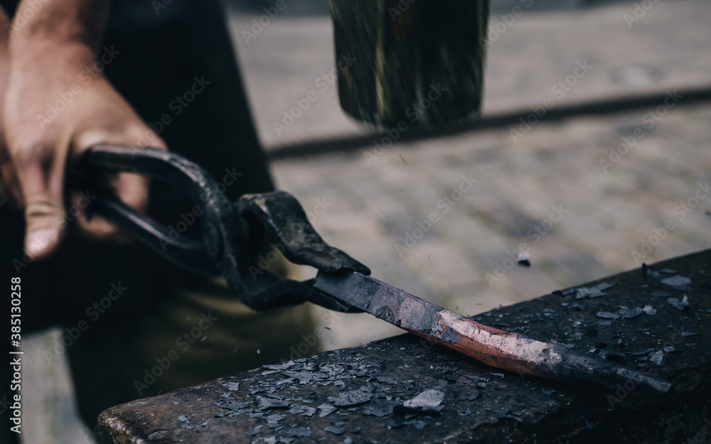 A blacksmith working with simple object by forging the metal. Flame ...