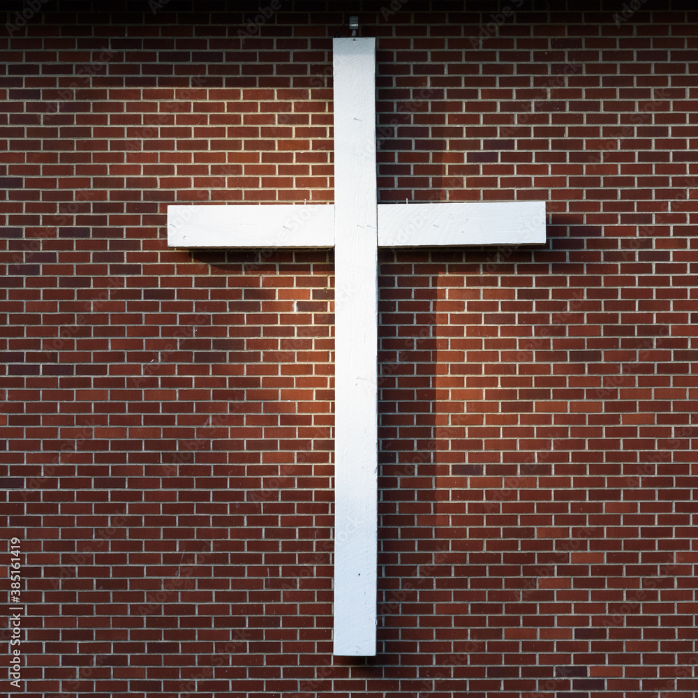 Simple white wooden cross on an exterior red brick wall, sunbeam on the ...