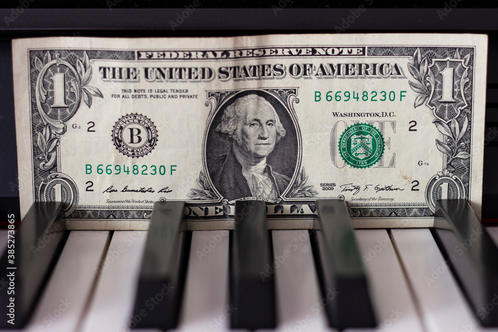 One dollar banknote lying on the piano keys. The dollar as a symbol of ...