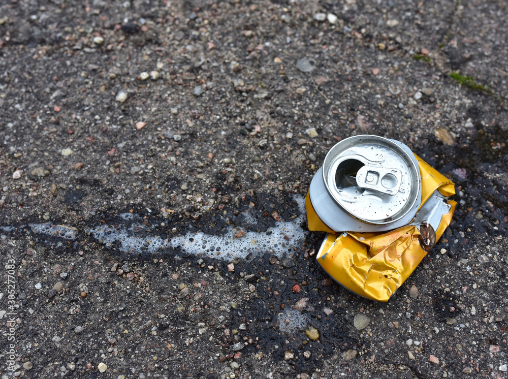 Crumpled a beer can on asphalt with spilled alcohol. Discarded broken ...