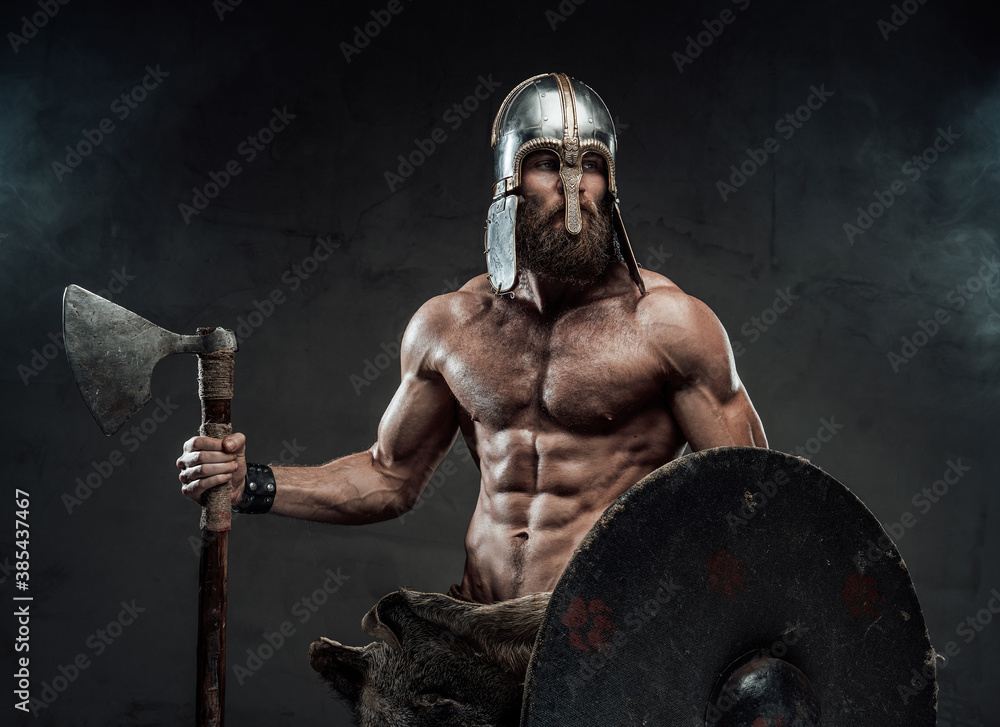 Haired and muscular viking with beard and helmet on him posing holding ...
