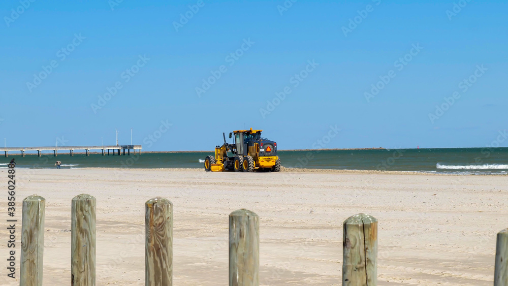Wood piling posts near beach with yellow road grader leveling sand on ...