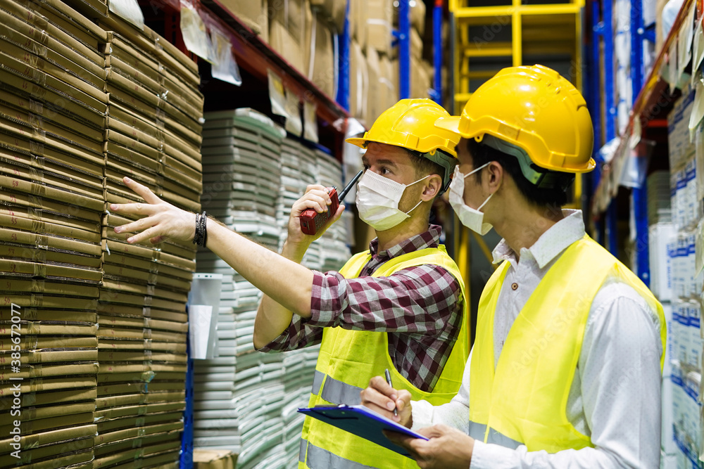 Warehouse manager and staff with safety helmet pointing towards shelf ...