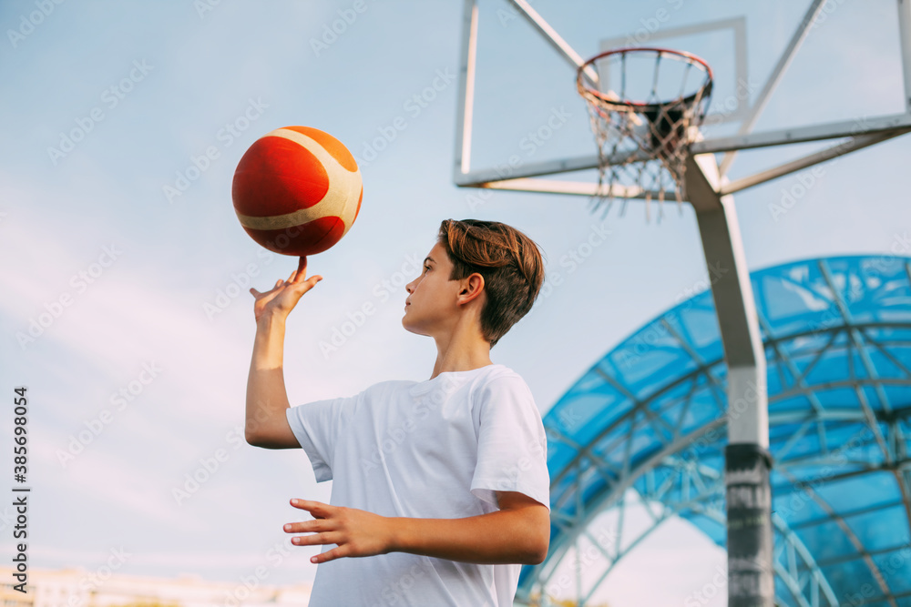 A young teenage basketball player in a white t-shirt stands on the ...