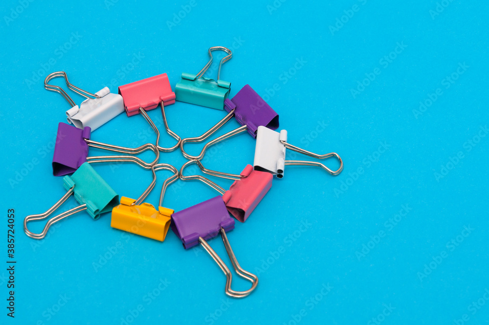 Five binder clips of different colors on a blue paper background making ...