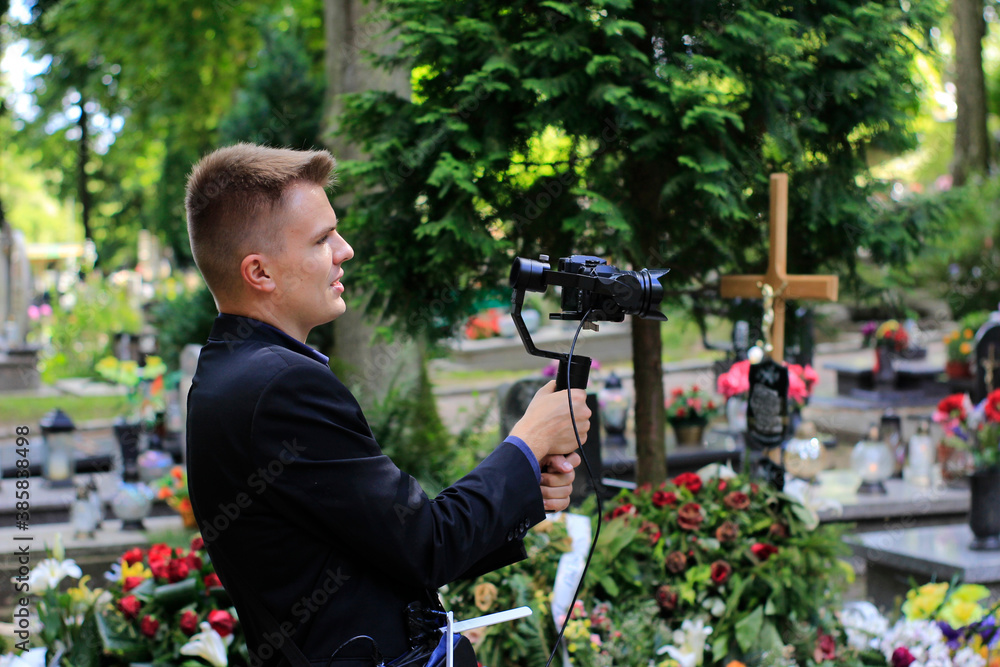 Elegant man in suit is recording grave with cross full of flowers ...