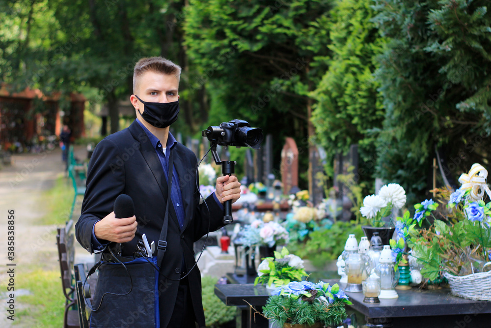 Elegant man in suit is recording grave with cross full of flowers ...