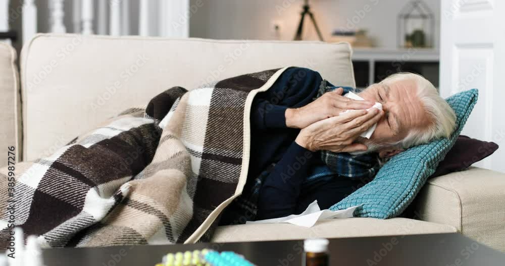 Sad Caucasian unwell grey-haired male lying on sofa in room and ...