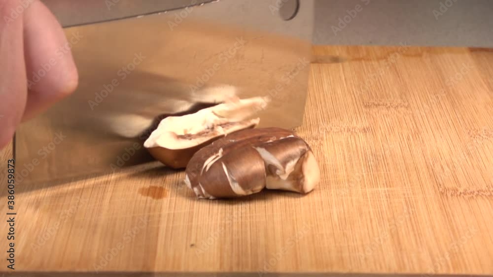 Hand with large cleaver roughly chops mushroom into large uneven chunks ...