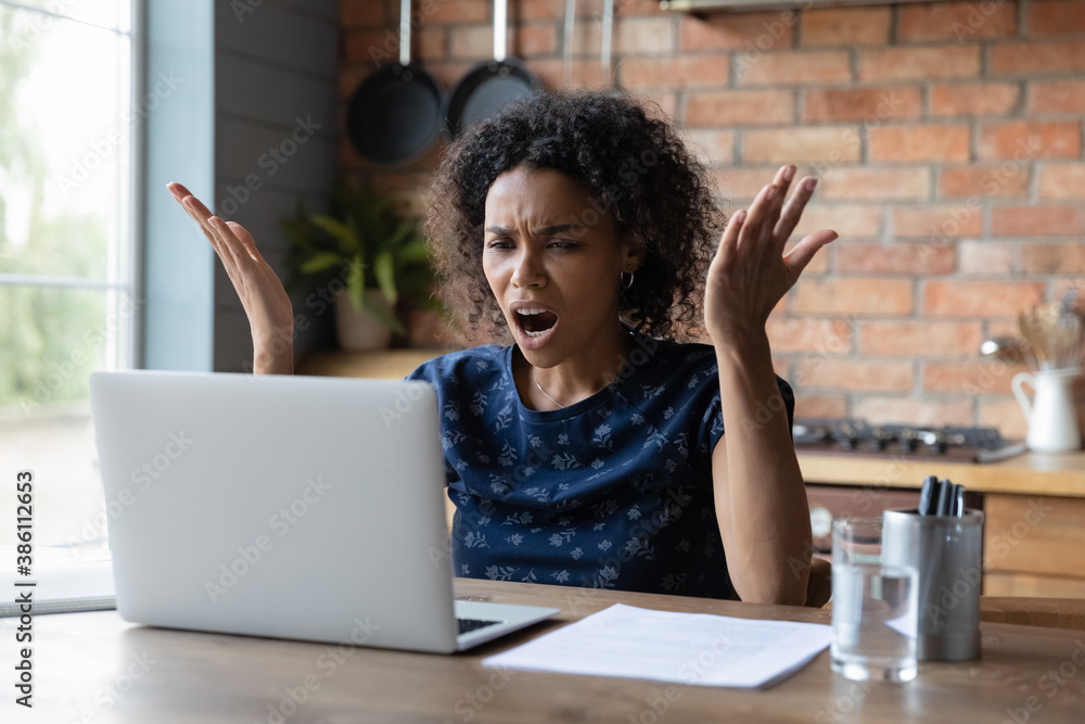 Angry young African American woman look at laptop screen distressed ...