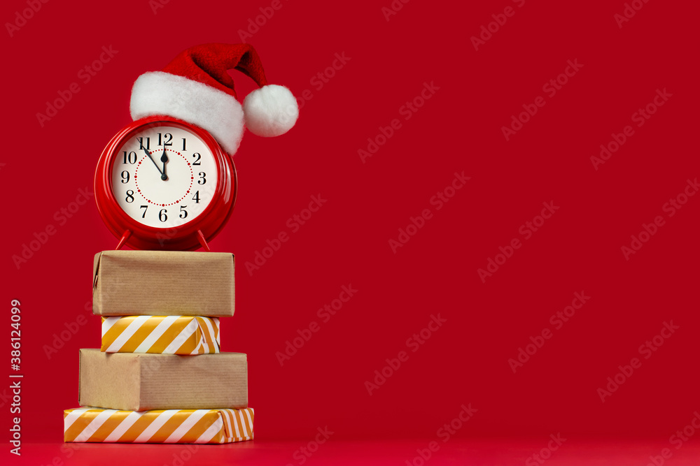 Red alarm clock in Santa Claus hat on gift boxes. Red background ...
