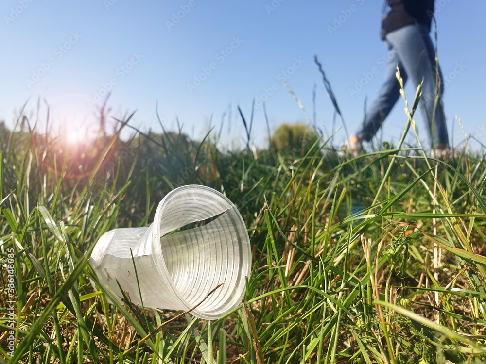 Used plastic cup in the grass and a blurred figure on the background ...