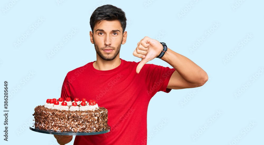 Young handsome man celebrating birthday with cake with angry face ...