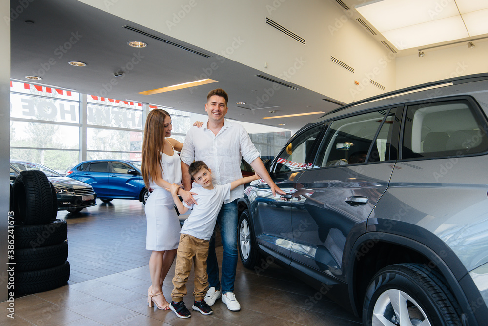 A happy young family chooses and buys a new car at a car dealership ...