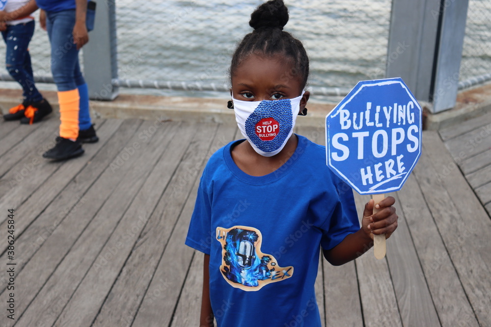 Young Kid wearing face mask and holding sign with words Bullying Stop ...