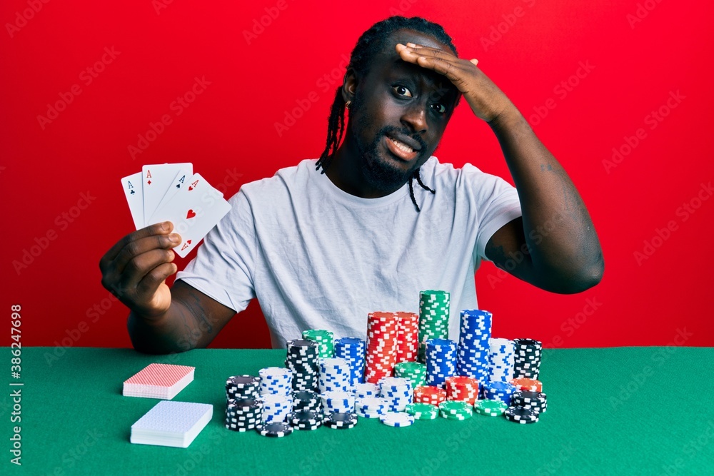Handsome young black man playing poker holding cards stressed and ...