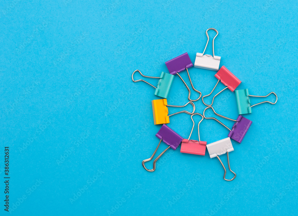 Five binder clips of different colors on a blue paper background making ...