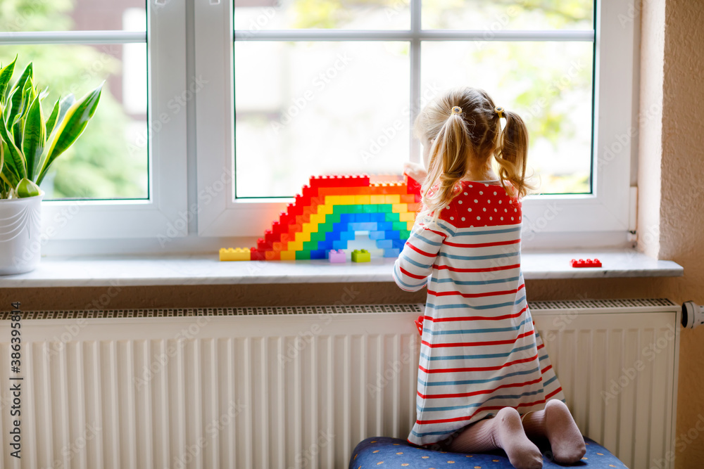 Cute little toddler girl by window create rainbow with colorful plastic ...