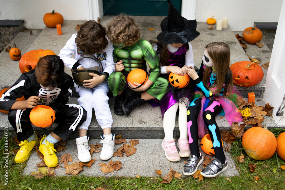 Group of trick-or-treating kids talking and sharing candies on a porch ...